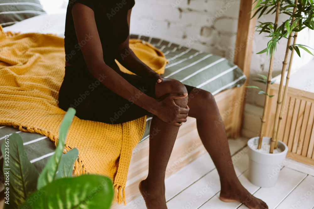 Afro american woman sitting in decorated studio and massaging knee cap ...