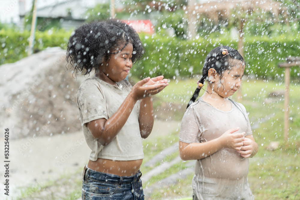 African American child girl and Asian child girl playing wet mud puddle ...