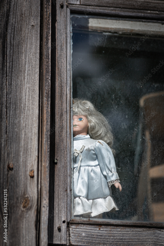 Scary doll looks out the window of an old house. Creepy girl doll in a ...