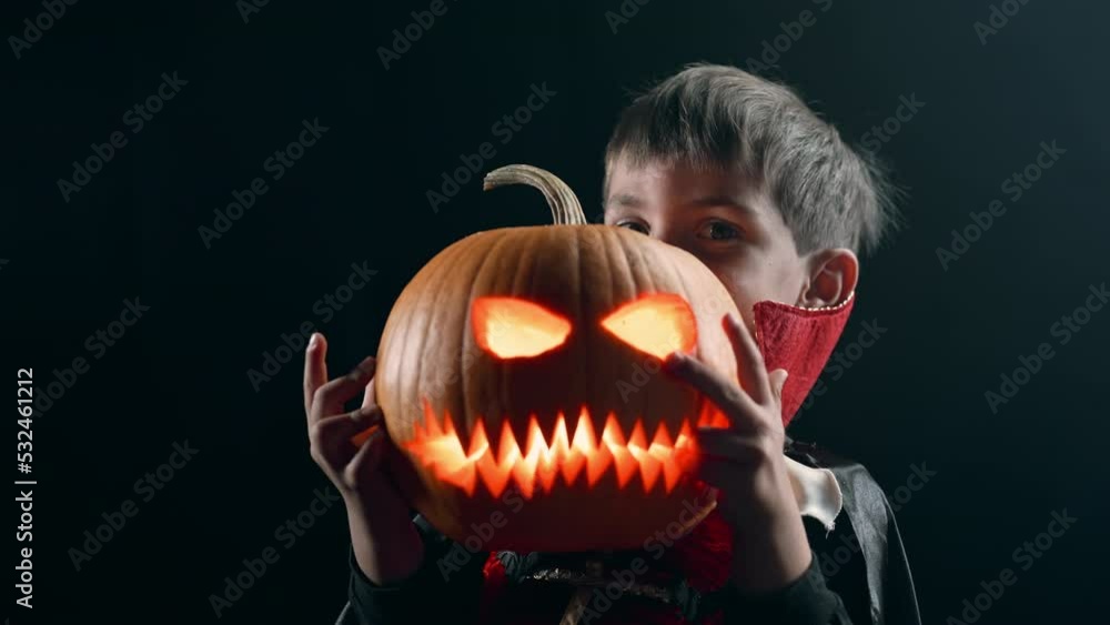 Little boy in vampire costume holding carved pumpkin on black ...