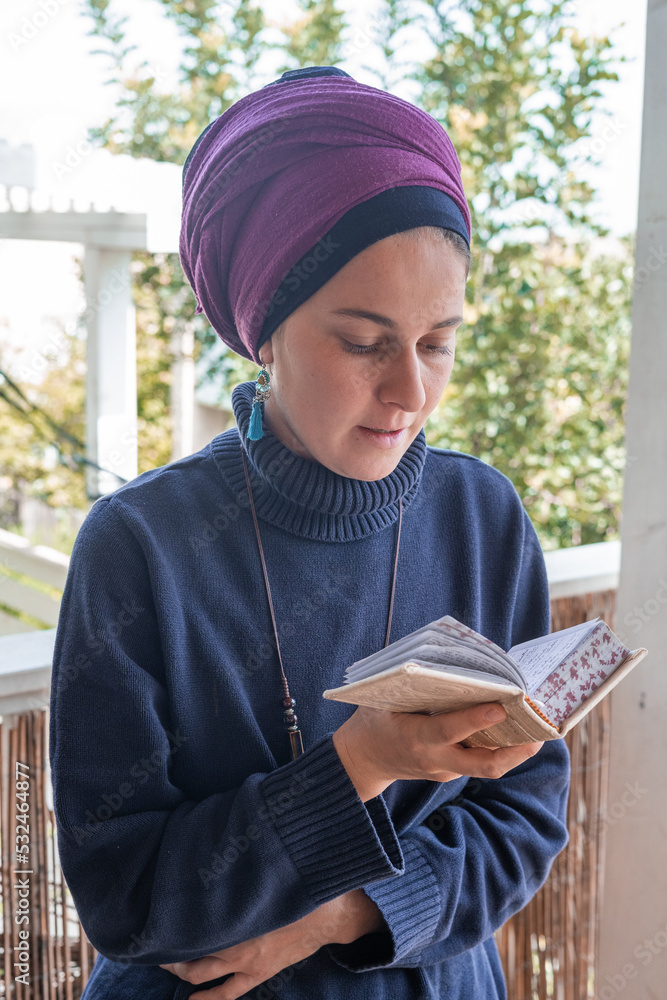 Young religious jewish woman with a covered head prays with a siddur in ...