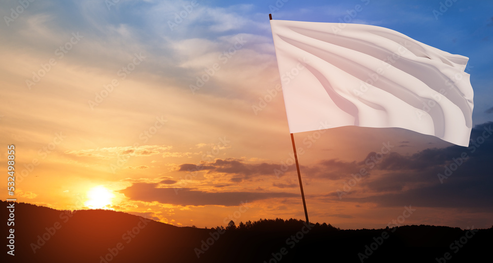 White flag waving in the wind on flagpole against the sunset sky with ...