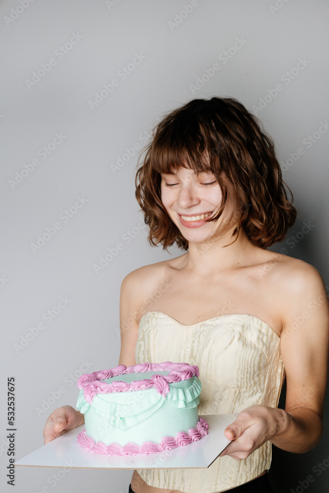 Happy curly girl in beige corset is holding a colourful birthday cake ...