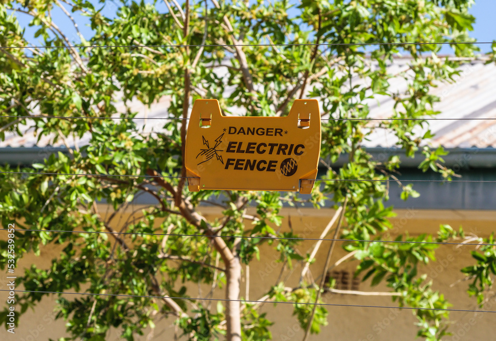 Electric fence and yellow warning sign, near a building in African town ...