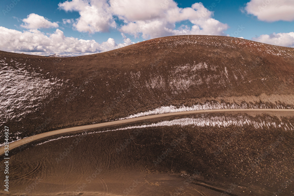Montaña de color marrón café, carretera de ripio y cielo azul con nubes ...