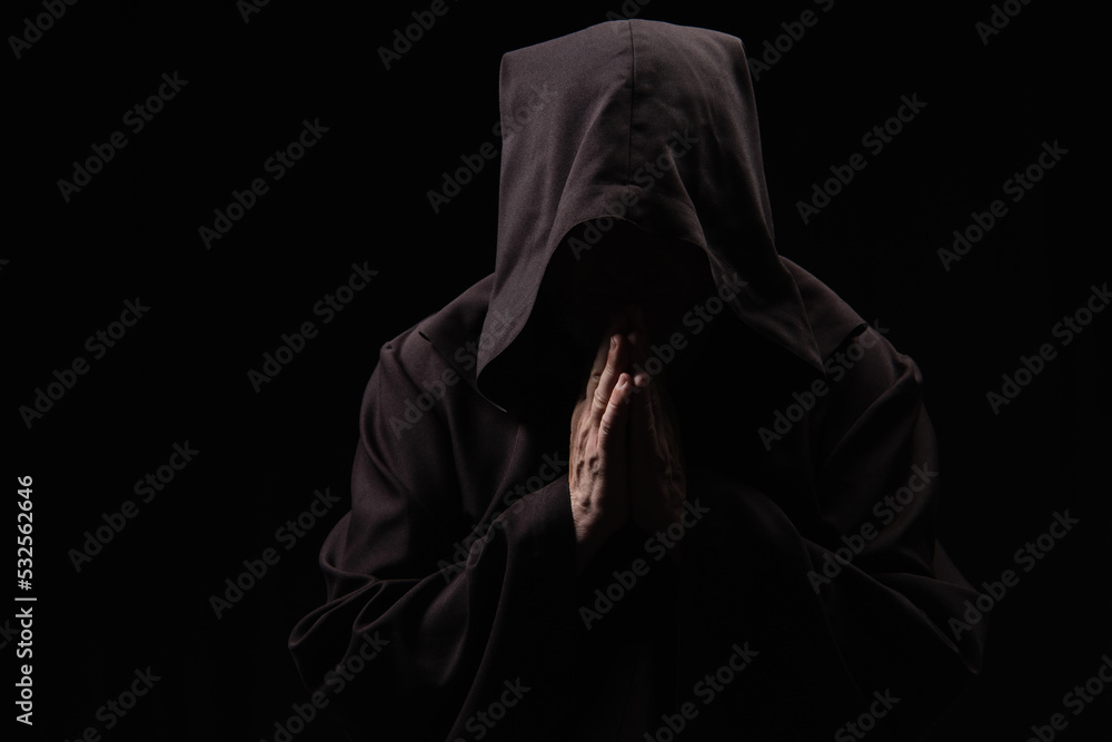 medieval monk with face under dark hood praying isolated on black ...