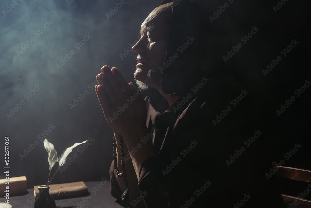 medieval monk praying near inkpot and manuscript on black background ...