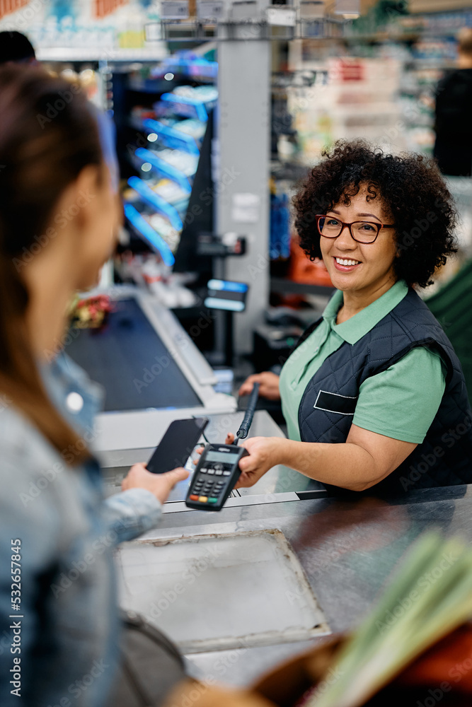 Happy cashier holds credit card reader while customer is paying with ...