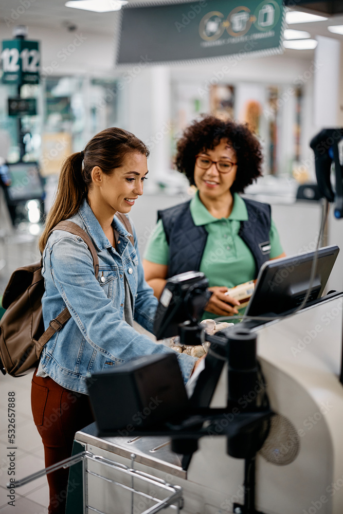 Smiling supermarket customer using self-service till with help of ...