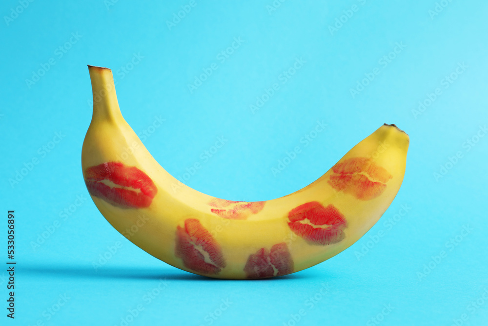Banana covered with red lipstick marks on light blue background ...