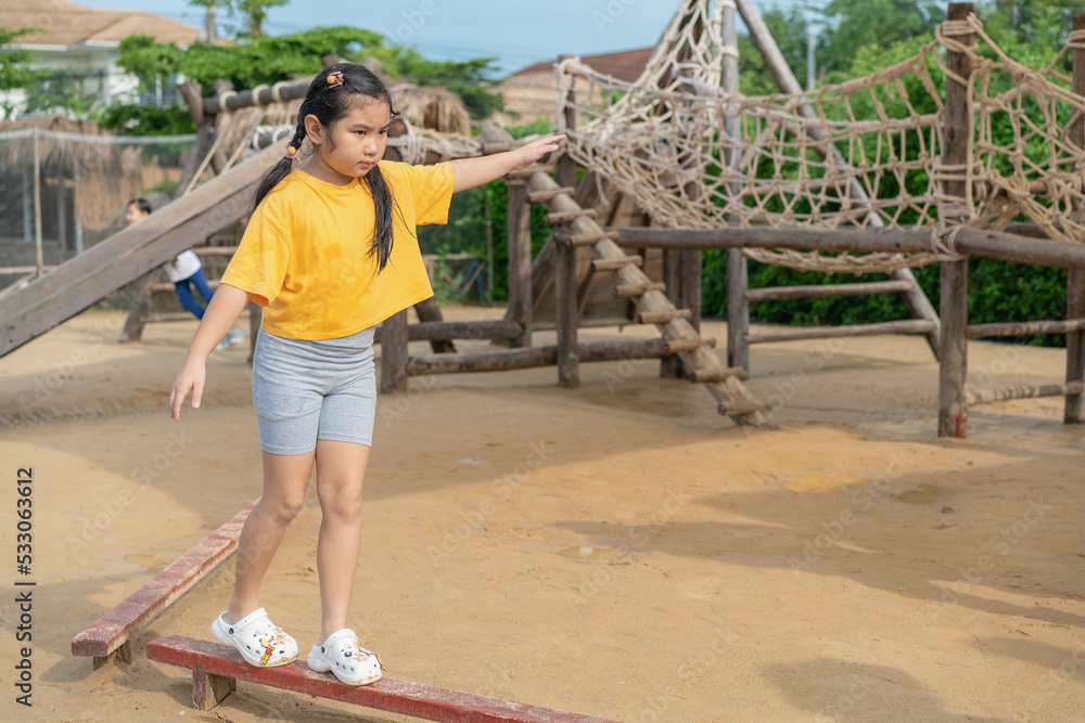 Asian little girl walking on the balance beam at outdoor playground ...