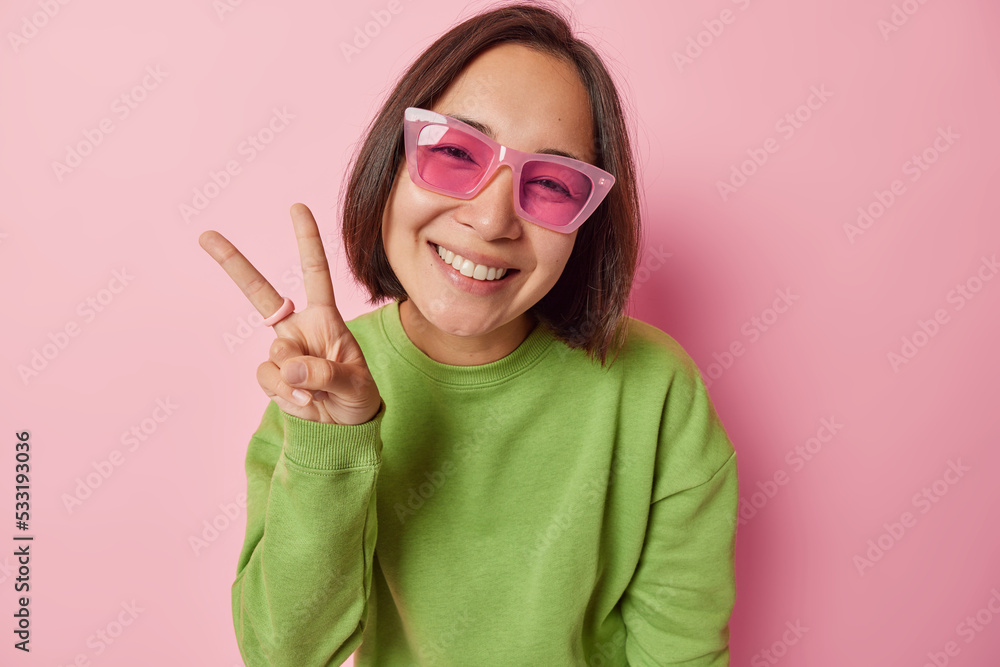 Positive Asian woman with dark hair makes peace sign enjoys amusing ...