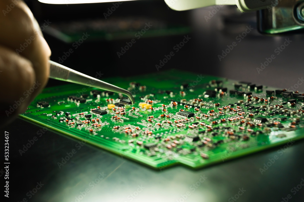 Manual assembly of electric components onto green PCB. Closeup shot of ...