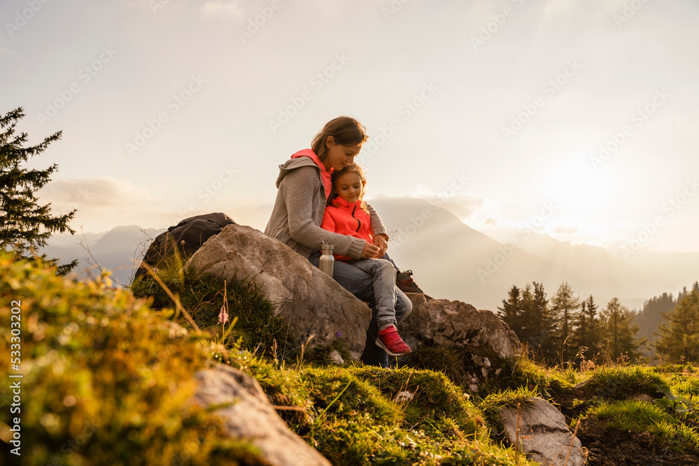 Smiling mother with daughter sitting on rock Stock Photo | Adobe Stock