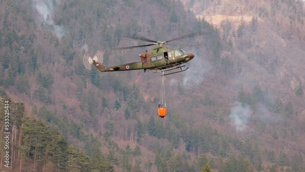 Firefighting helicopter with a bucket suspended on a cable, collecting ...