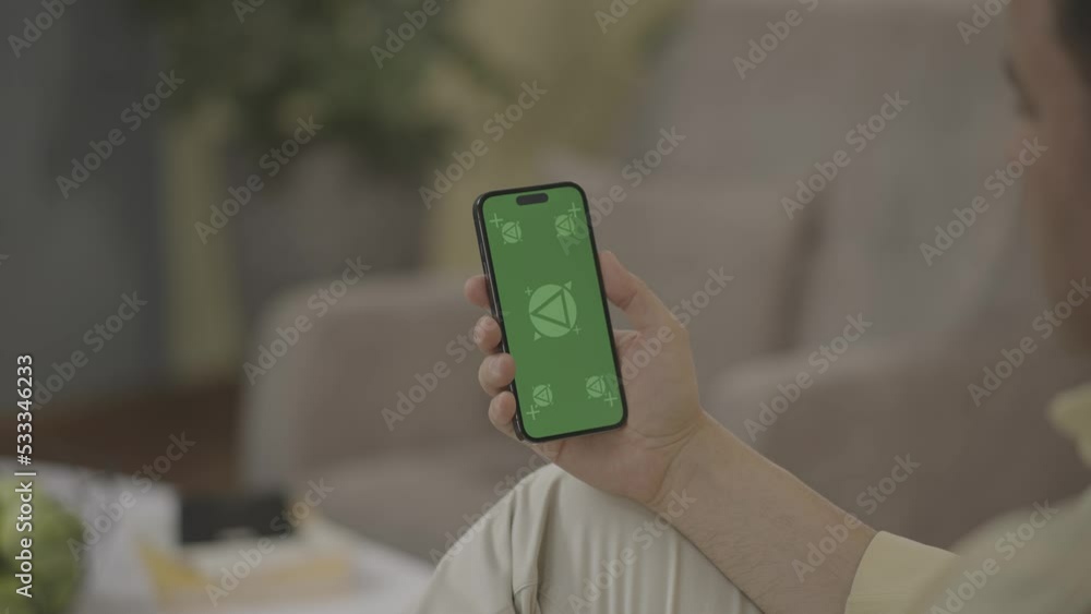 Man watching iPhone 14 pro green screen mock-up on sofa relax in home ...