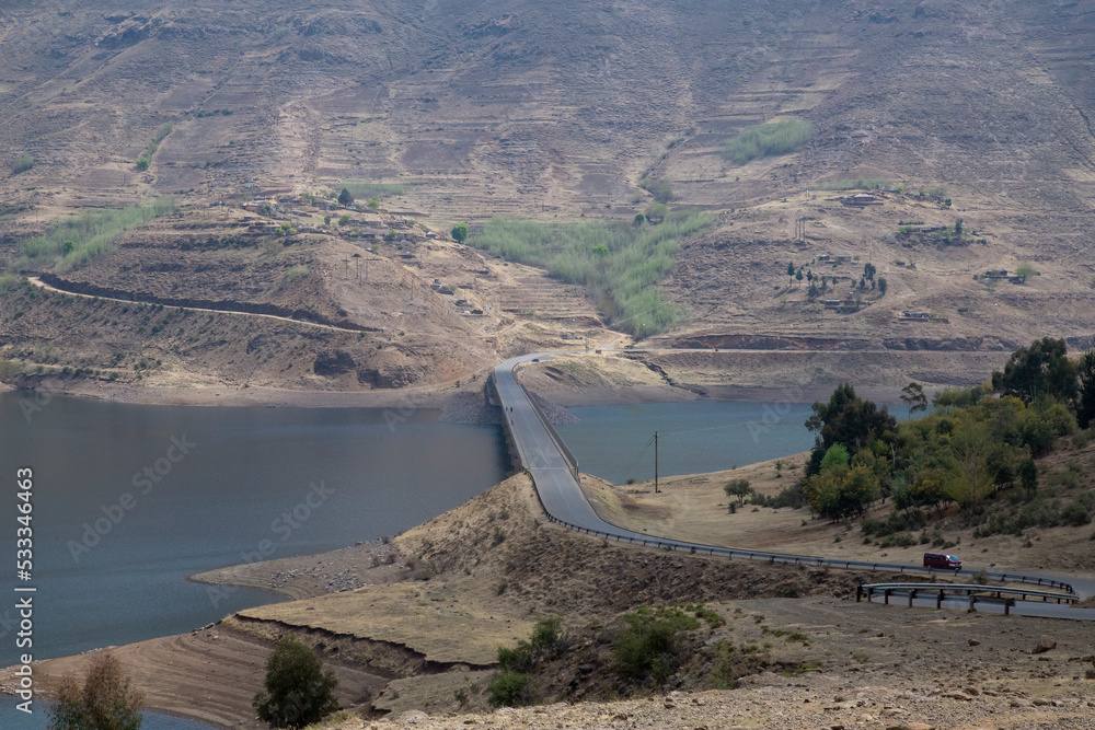 dam with dam wall bridge winding through mountains clouds and blue ...