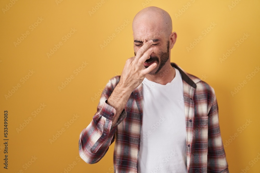 Hispanic man with beard standing over yellow background smelling ...