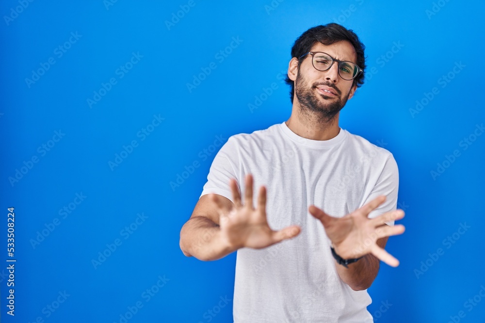 Handsome latin man standing over blue background disgusted expression ...