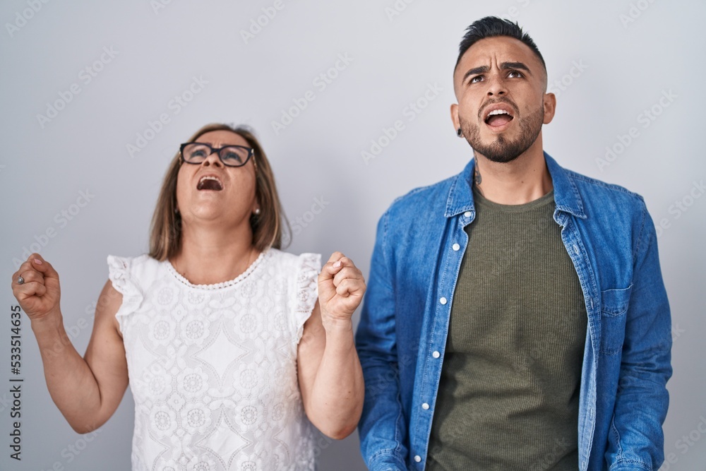 Hispanic mother and son standing together angry and mad screaming ...