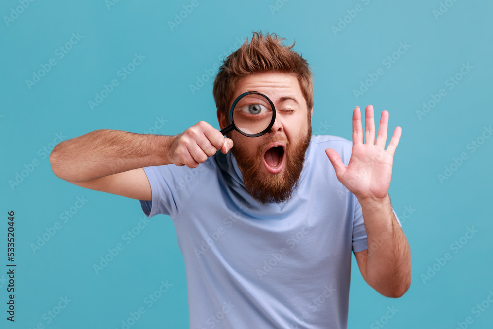 Portrait of funny bearded man holding magnifying glass and looking at ...