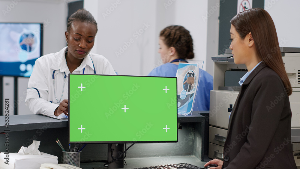 Diverse medical team using computer with greenscreen at reception ...