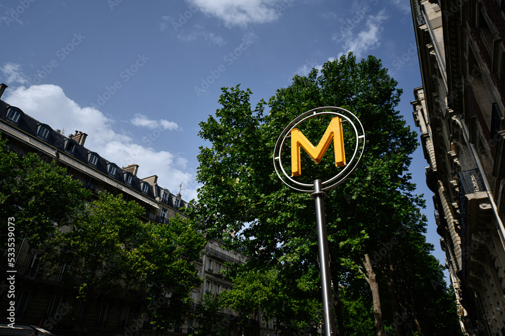 Sign with the subway logo (yellow symbol) in front of a parisian metro ...