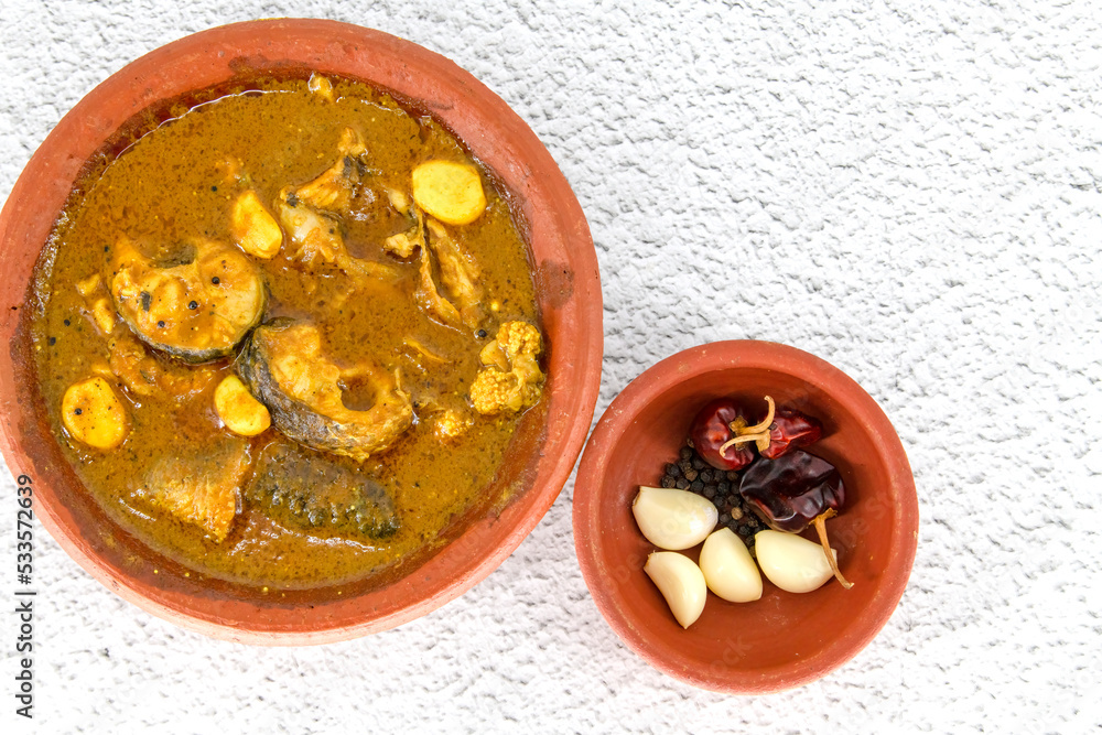 Fish curry served in traditional mud pot with fish curry ingredient ...