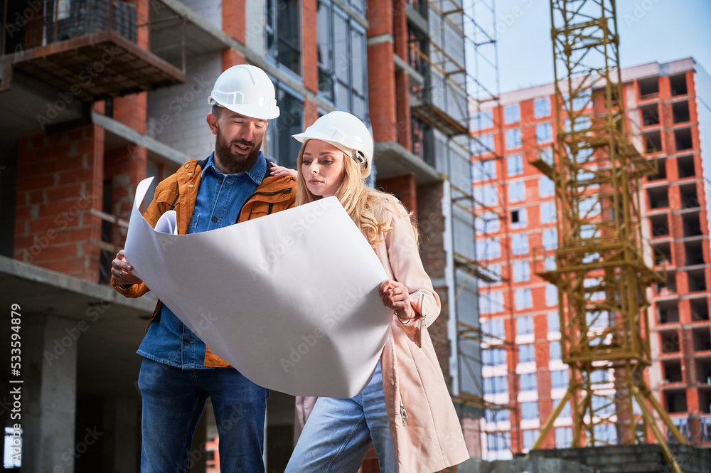 Couple in safety helmets studying architectural drawings outside ...
