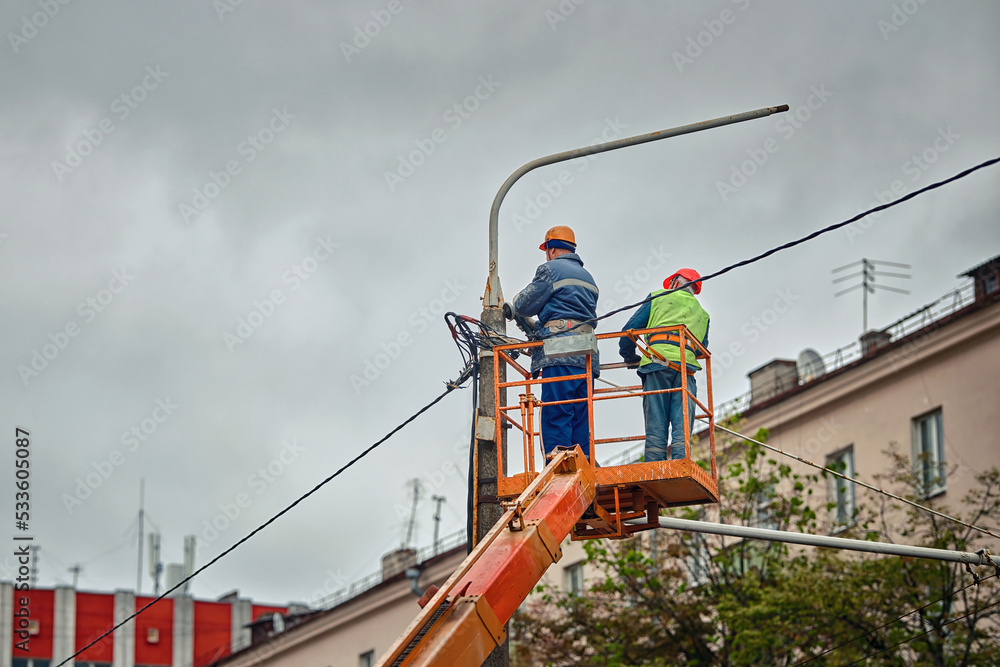 Workers in lift bucket repairing street lamp pole. Municipal work ...