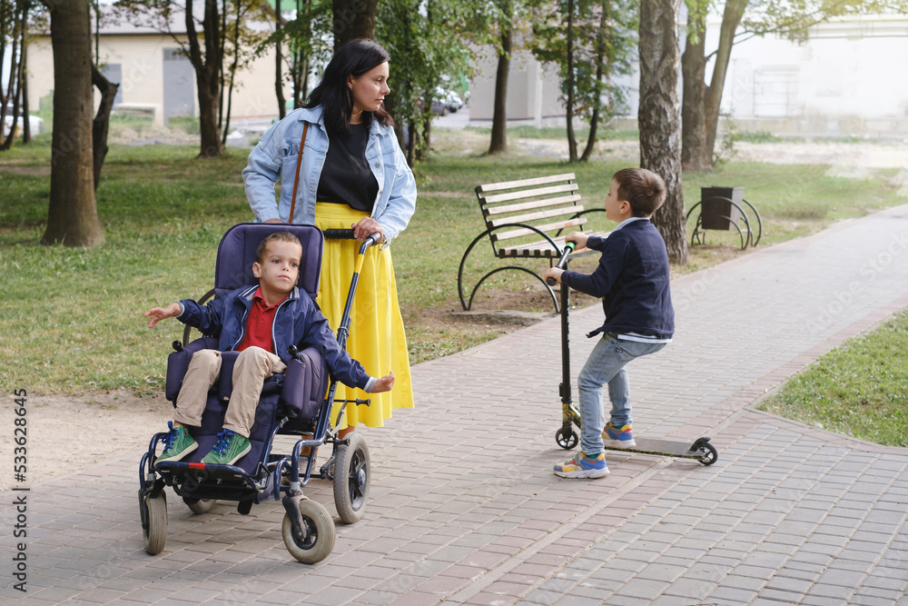 Family with cerebral palsy child on special wheelchair walking outdoors ...