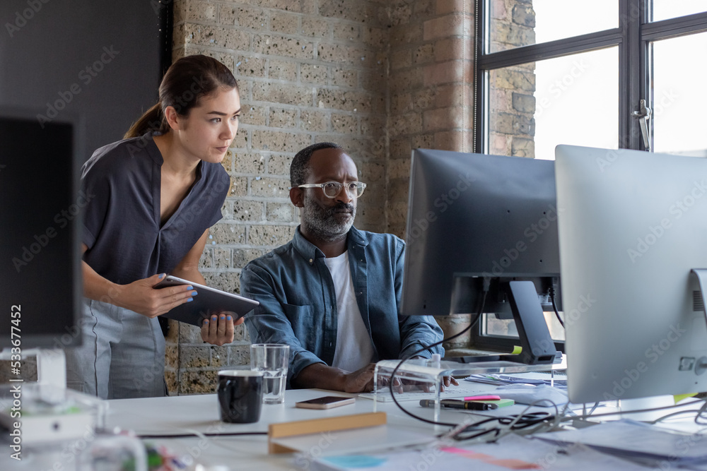 Coworkers working together on a digital tablet and a desktop computer ...