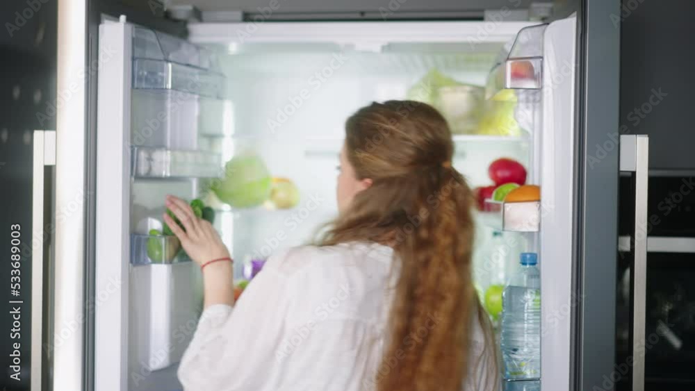 Vidéo Stock Young woman taking vegetables from fridge and has fun ...
