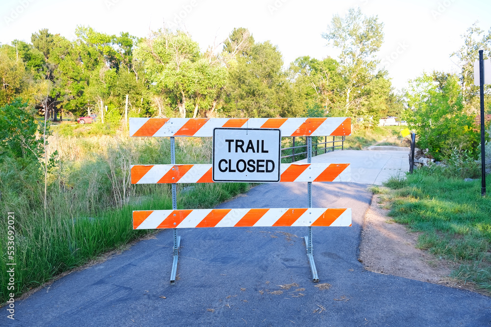 Trail closed warning sign with white and orange stripes along walking ...