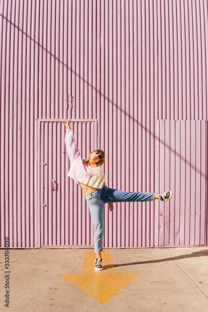 Woman With Hand Raised Standing On One Leg Over Arrow Symbol In Front Of Corrugated Wall Stock