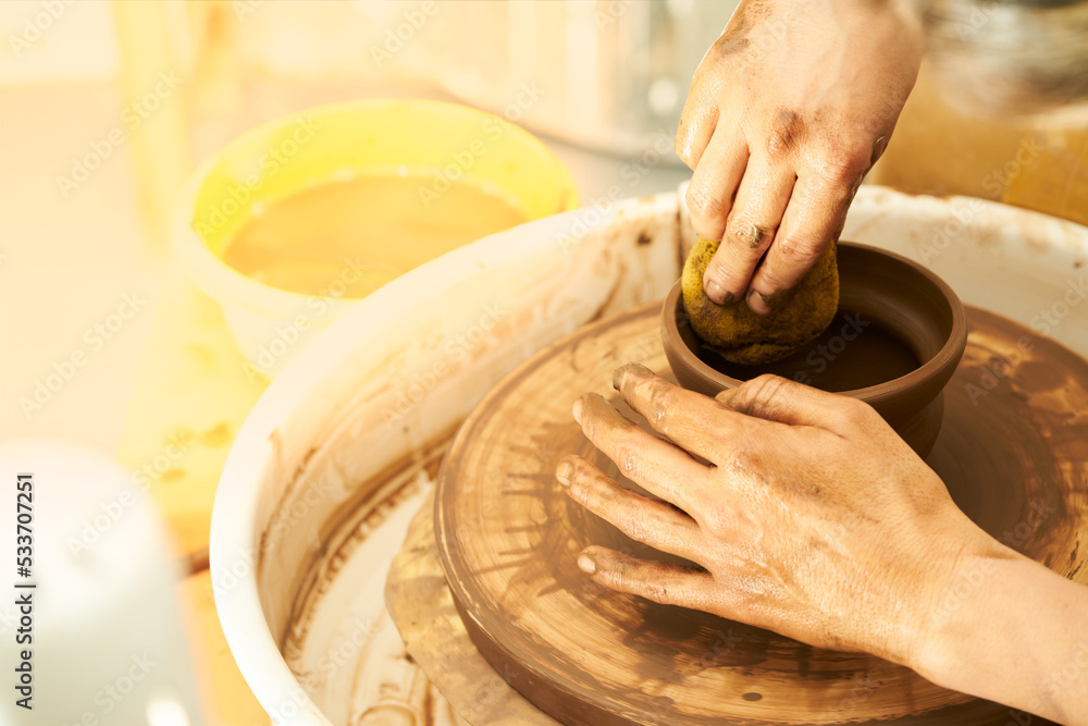 A Potter works with red clay on a Potter's wheel in the workshop..Women ...