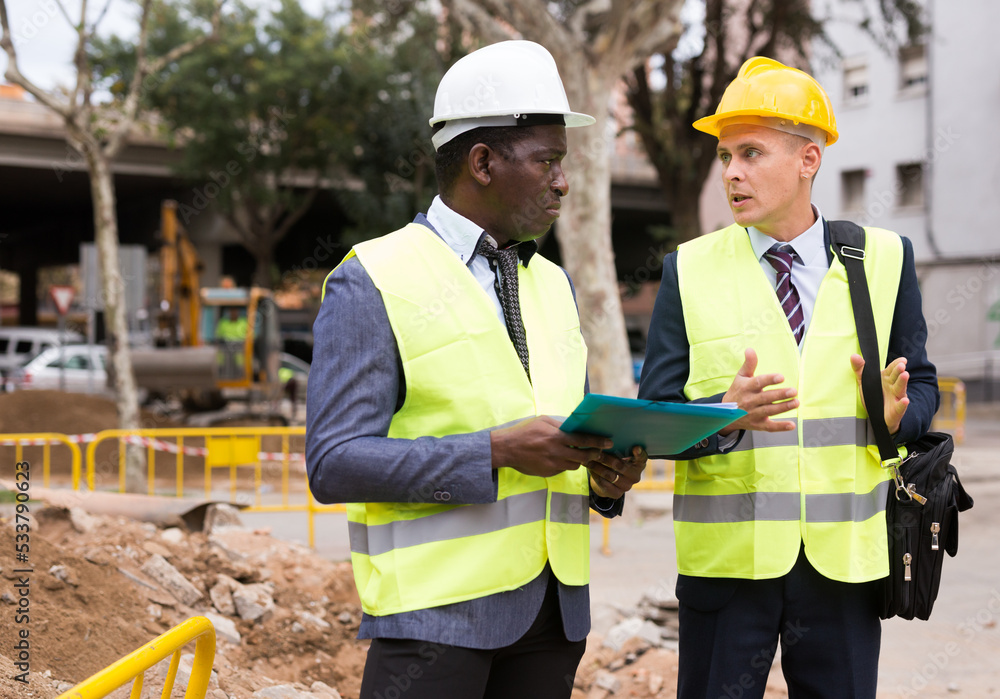Two men workers working at the laying paving slabs facility discuss the ...