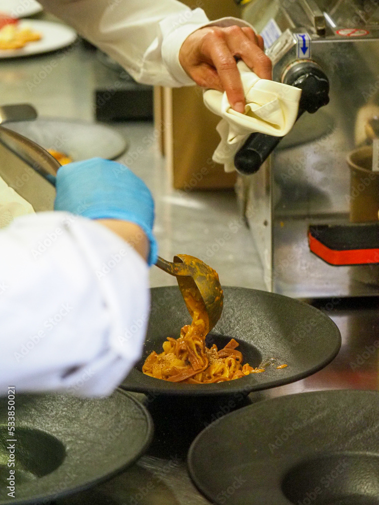 chef plating tagliatelle sauce pasta into black design dishes - mise en ...