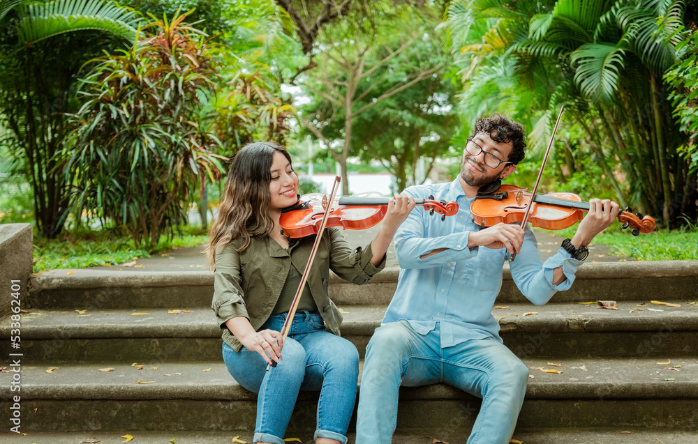 Portrait of two young violists playing violin sitting on stairs outside ...