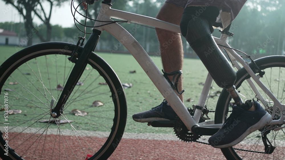 Person with prosthetic leg riding bicycle outdoors. A disabled athlete ...