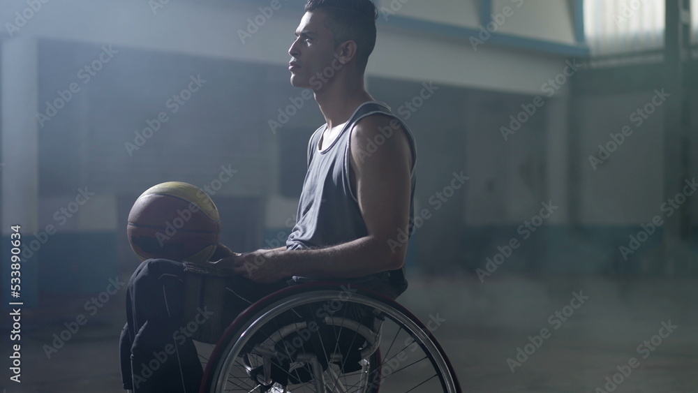 Disabled athlete in a wheelchair with dramatic lighting holding ball ...