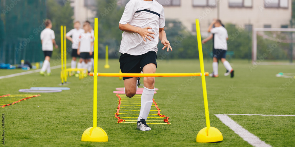 Young boy jumping over ladder and pole at a soccer training session ...