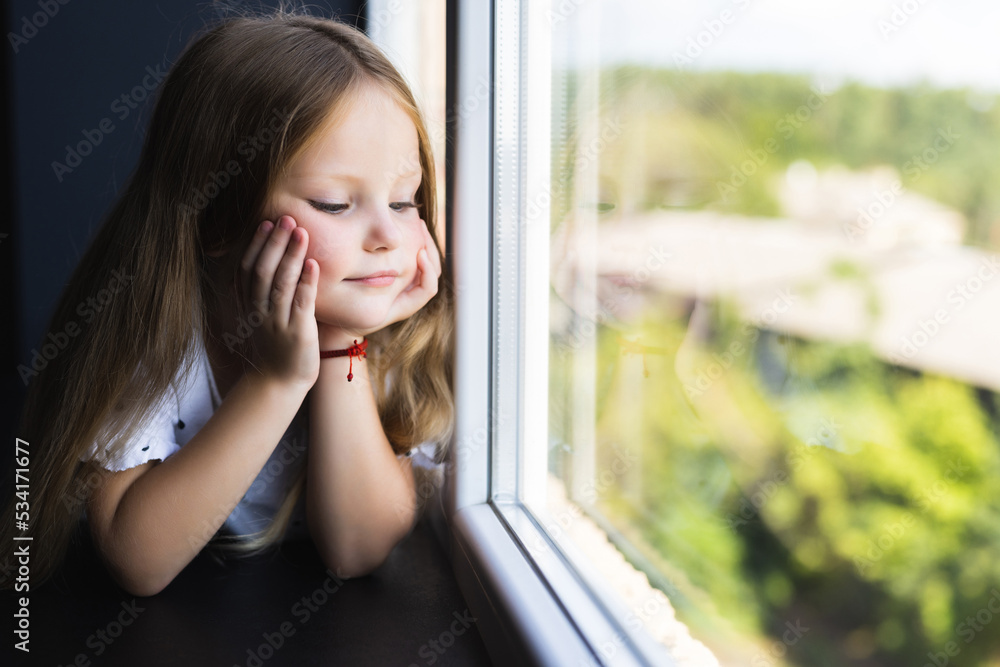 Beautiful little girl smiling and watching out the window. A child ...