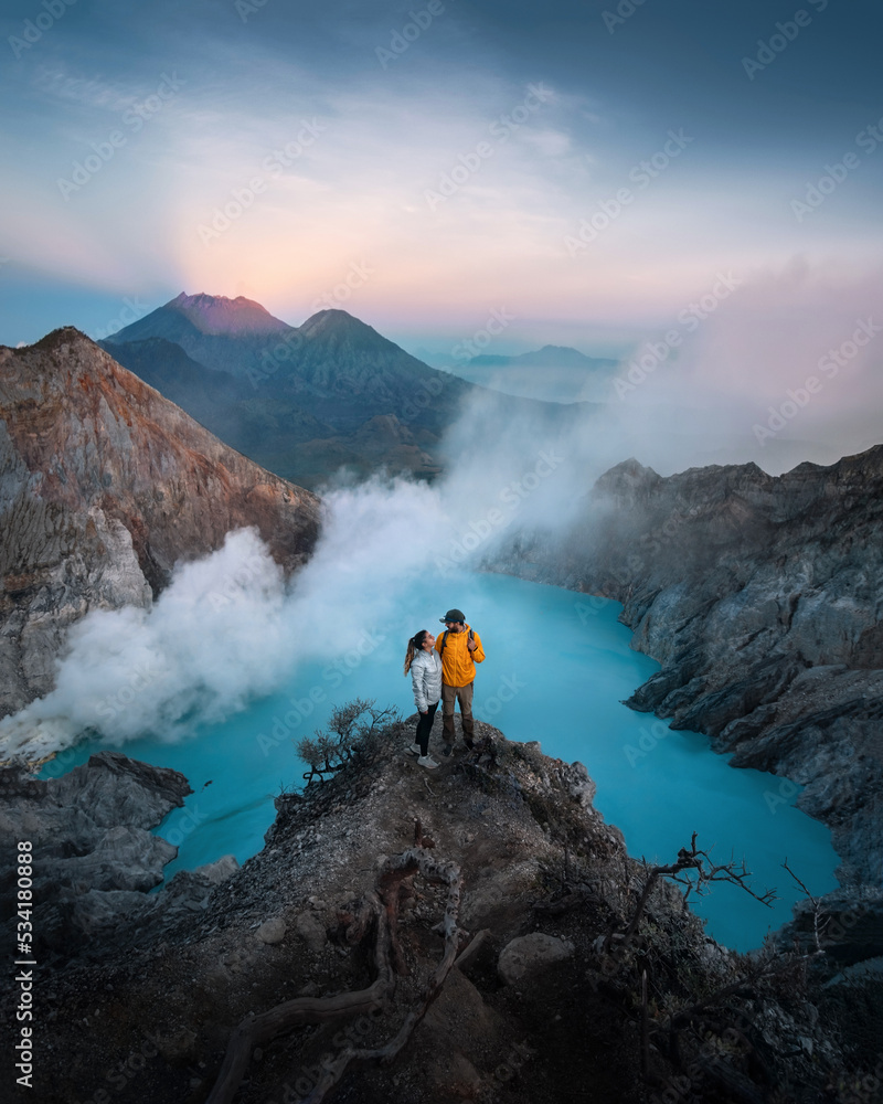 Traveler couple enjoy sunrise view on top of Ijen volcano with blue ...