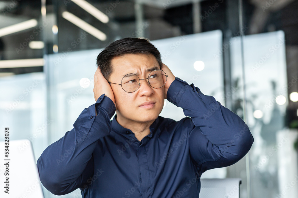Poster Noise in the office, Asian worker businessman covers his ears ...