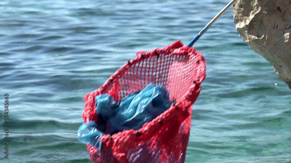 Volunteer with net catches garbage from water. Skimmer pulls plastic ...