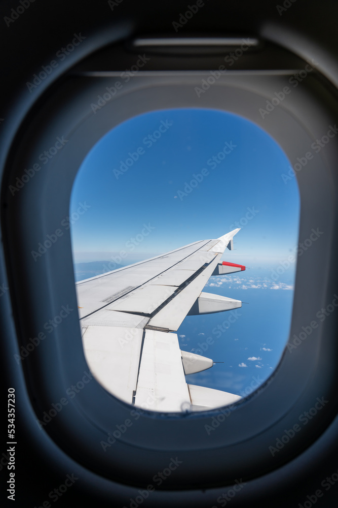 Airplane wing seen through a airplane window as a frame in a blue sky ...