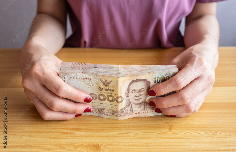An accountant woman with a pile of Thai baht banknotes. The baht is the ...