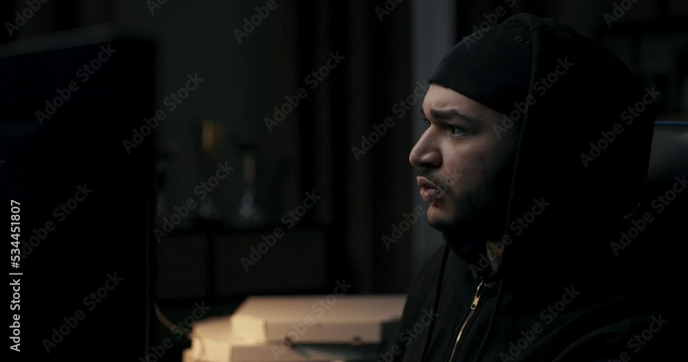 Hacker got new task. He is dressed in black clothes, sitting in dark ...