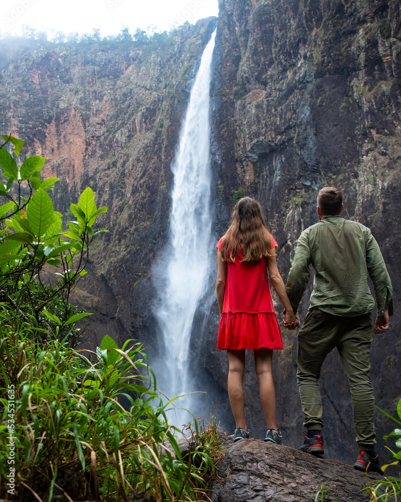 couple stands under huge waterfall holding hands, dramatic view of long ...